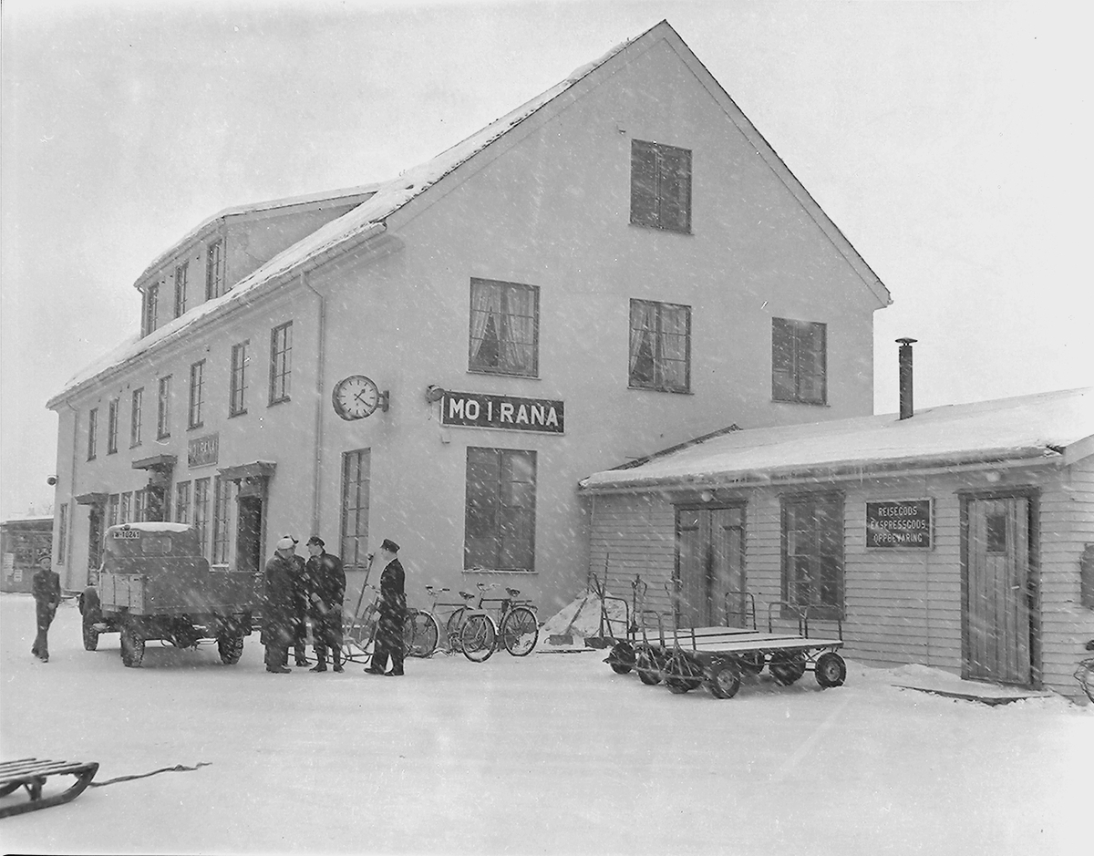 Jernbanestasjon. Mo i Rana stasjon. Lastebil. En gruppe mennesker står ...